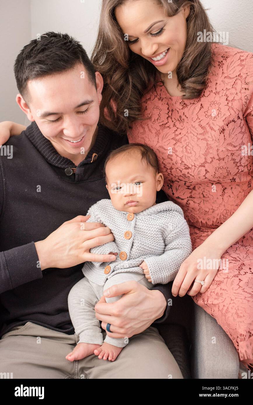 Happy parents sit closely with baby on their lap at home Stock Photo ...