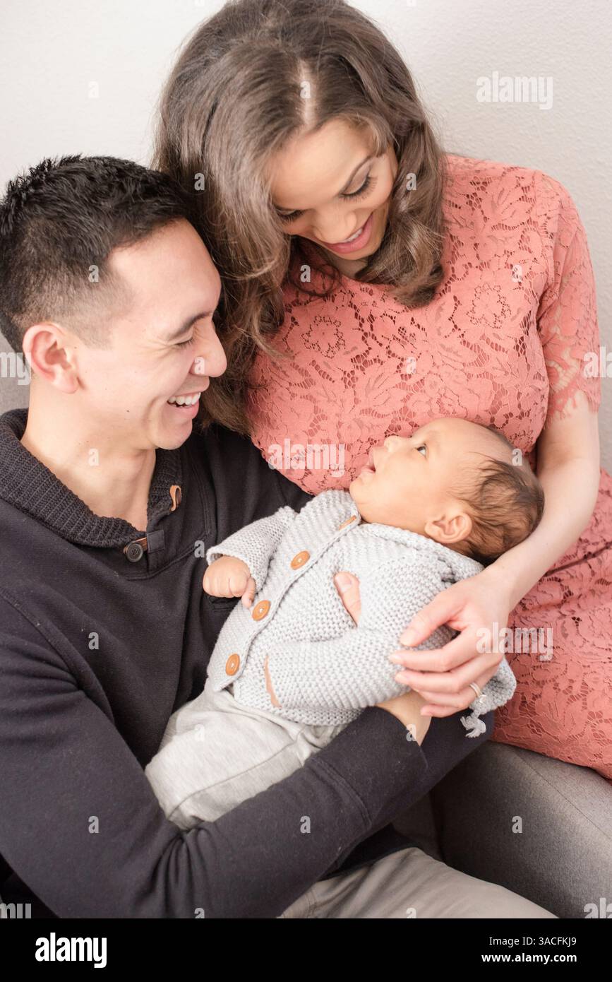 Baby smiles brightly while parents gaze down with joy and affection ...