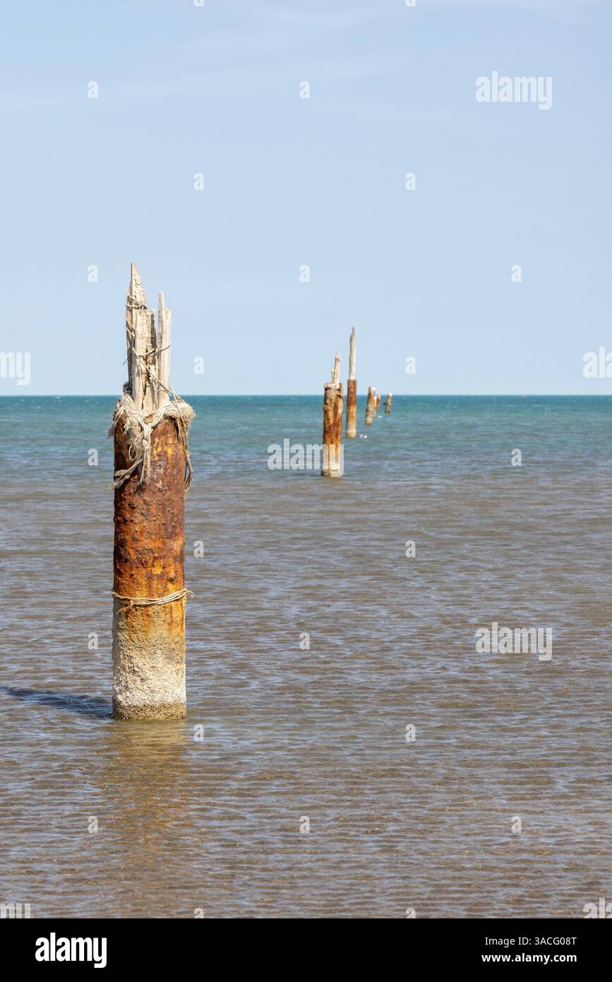 Weathered rusty posts rise from the shallow sea, embodying history ...