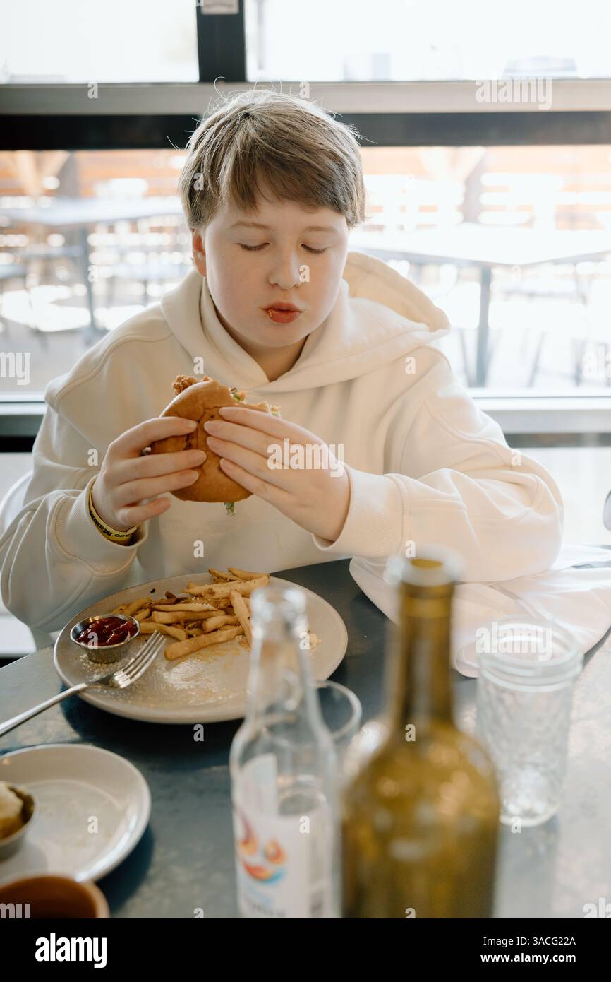 Teen boy mid-chew with burger at cafe Stock Photo - Alamy