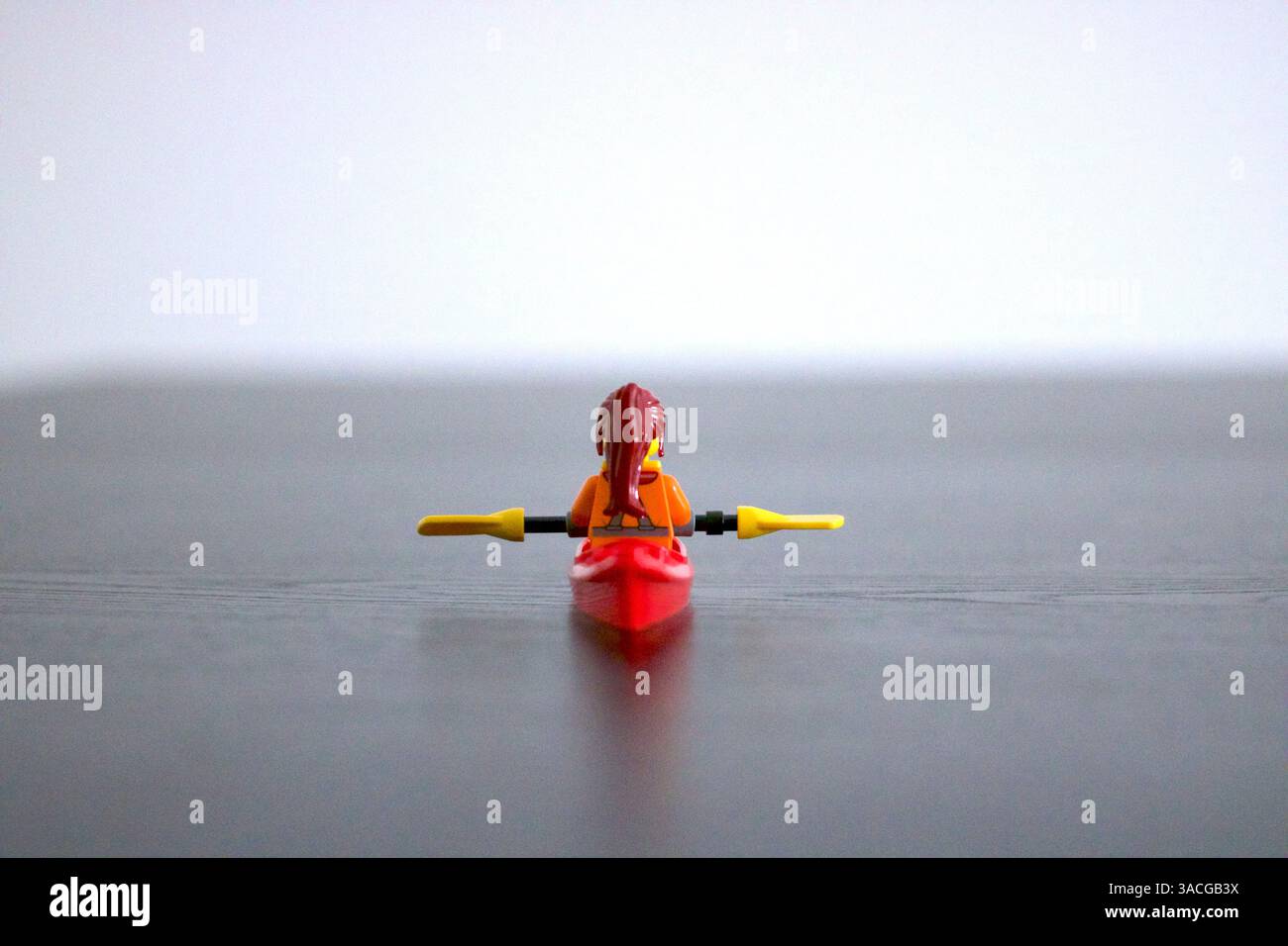 LEGO female figure rowing a bright orange kayak, captured from behind ...