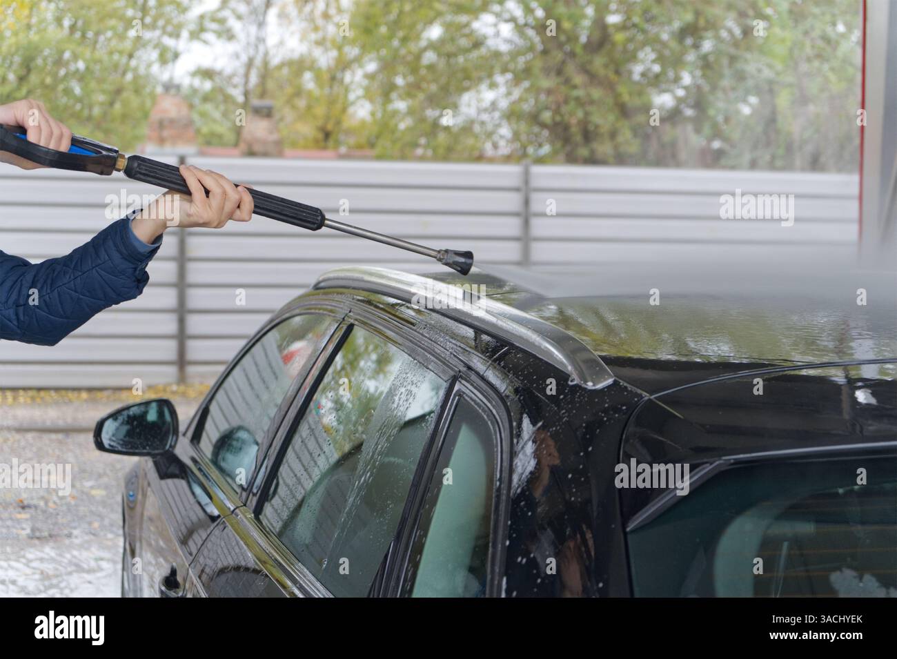 The image shows a person using a pressure washer to clean the roof of a ...