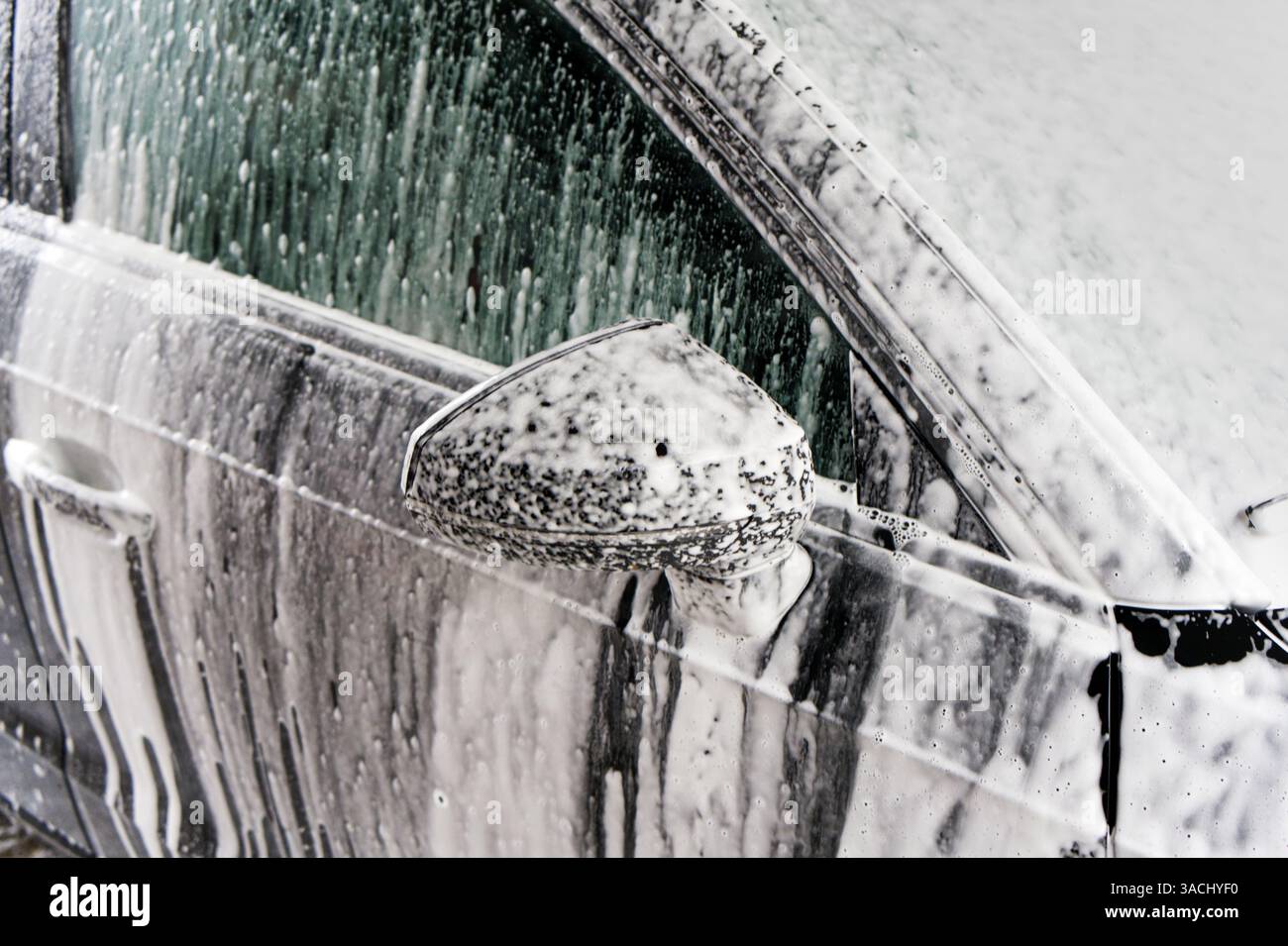 The image captures a car covered in soap suds, likely during a car wash ...