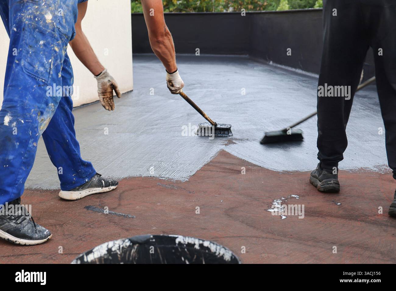Two builders construction workers with brushes applying waterproofing ...