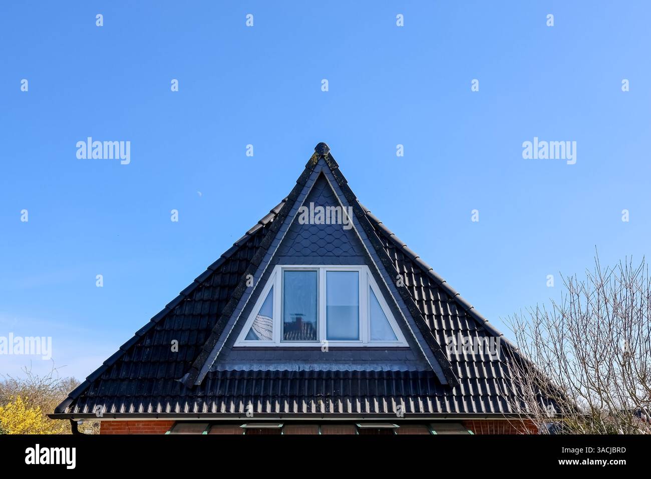 Triangular dormer window on a black tiled roof with blue sky, creating ...