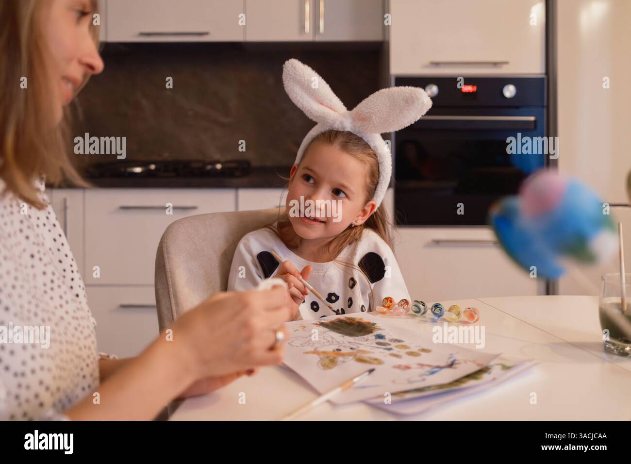 Mother and daughter painting Easter crafts together wearing bunny ears ...
