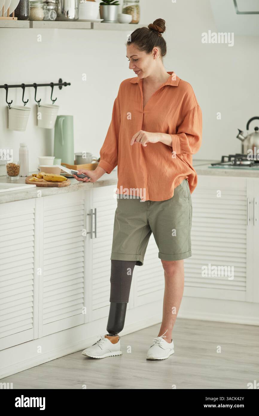 Vertical full length portrait of modern woman with disability cooking ...