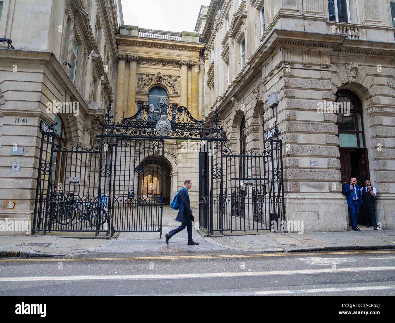 Pedestrian walks past wrought iron gates at Adams Court, City of London ...