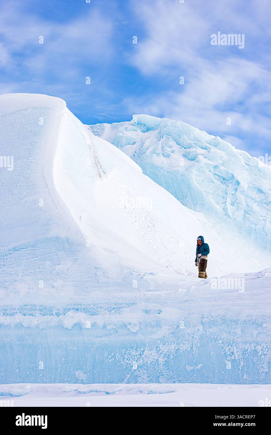Anonymous Inuit guide standing in front of an iceberg on a frozen fjord ...