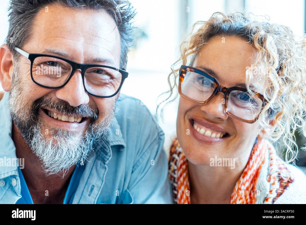 An adult couple in their late 40s, wearing glasses, smiling while ...