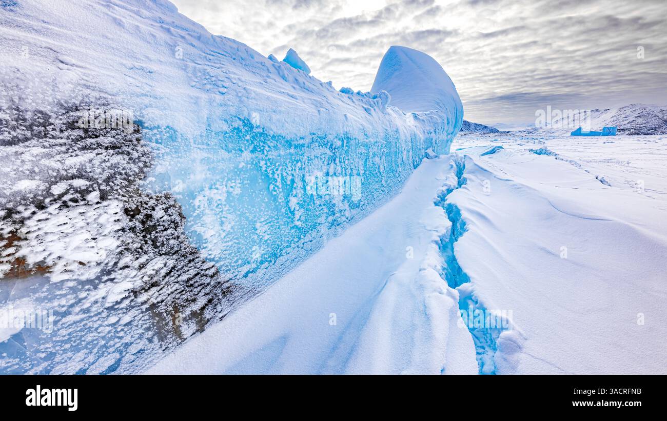 A crevasse opens up in the ice in front of icebergs and mountains ...