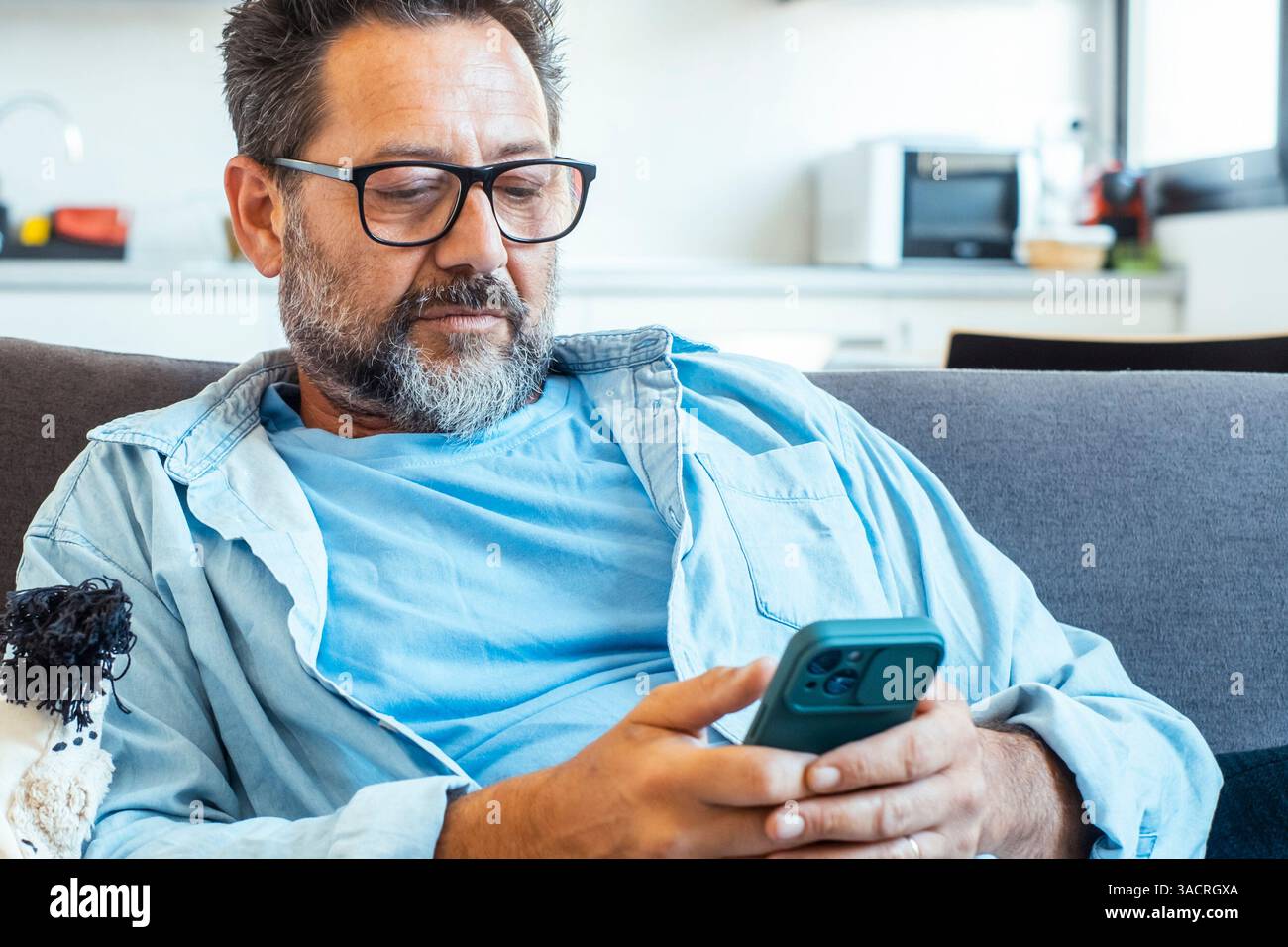 Pensive serious young man sit on sofa at home text message on modern ...