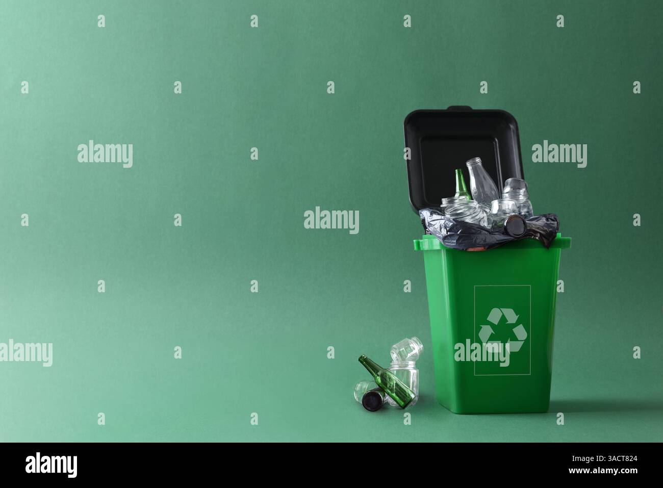 Green trash container with recycling symbol filled with glass objects ...