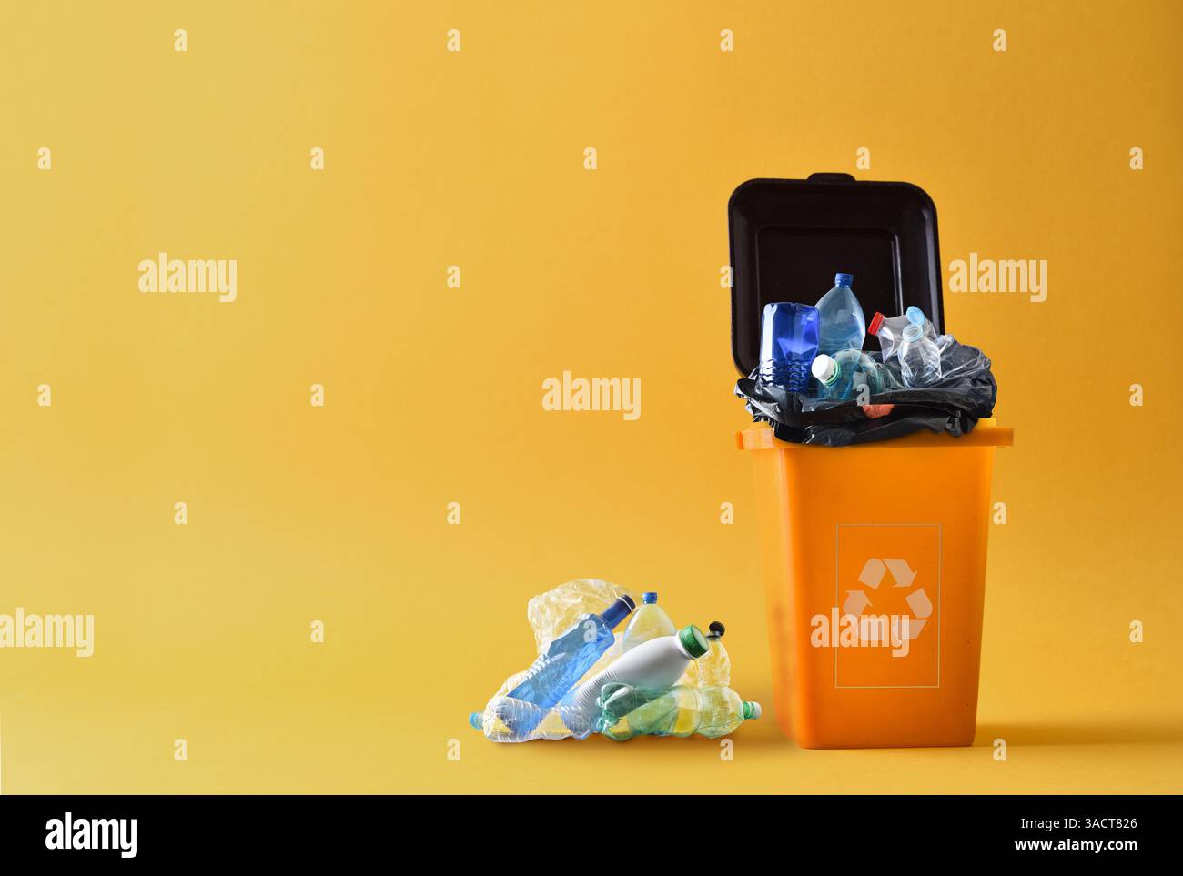 Yellow trash container with recycling symbol filled with plastics and ...