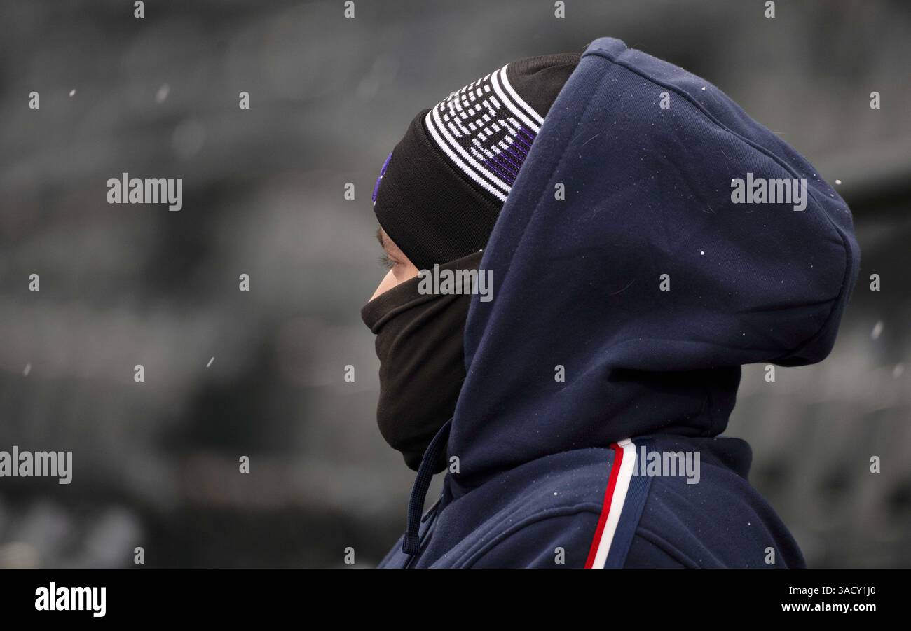 A fan sit in the stands of Coors Field as the snow begins to fall ...