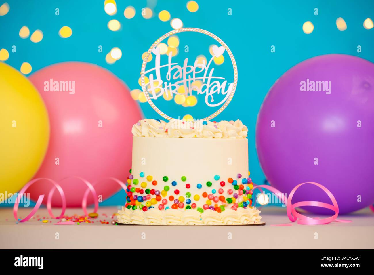 Tasty bento cake with colorful sprinkles, topper and balloons on table ...
