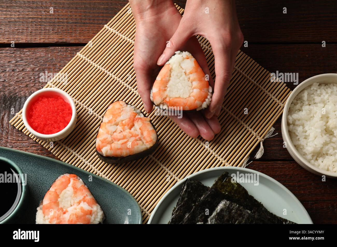 Woman holding tasty onigiri (Japanese rice ball) with shrimp at wooden ...