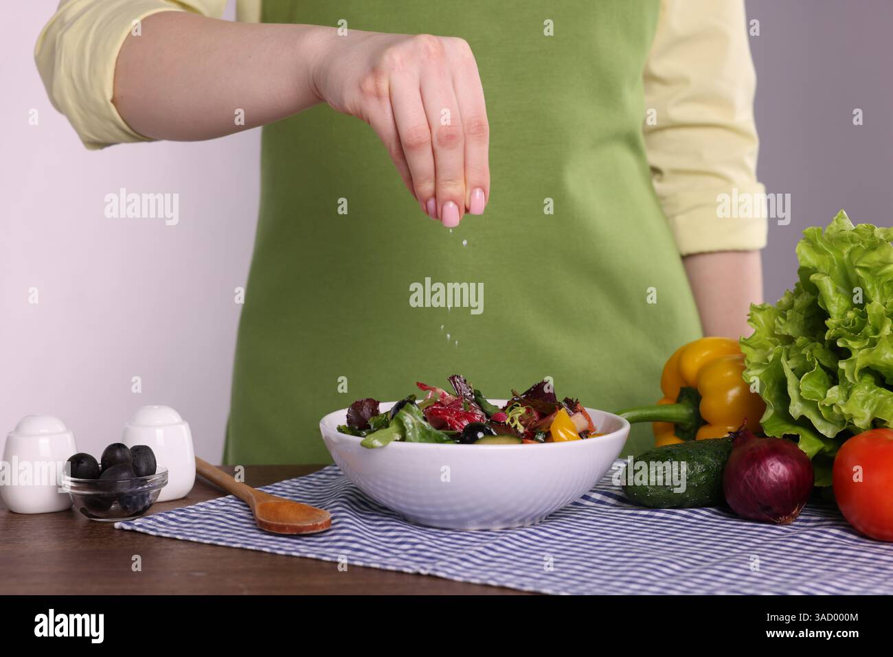 Woman salting tasty salad at wooden table against white background ...