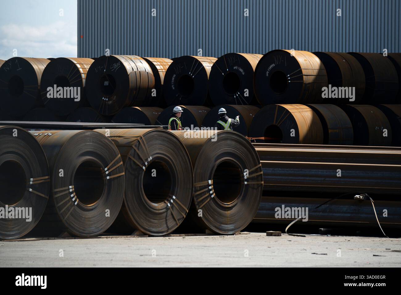 Personnel walk among steel coils and beams at a shipping terminal in ...