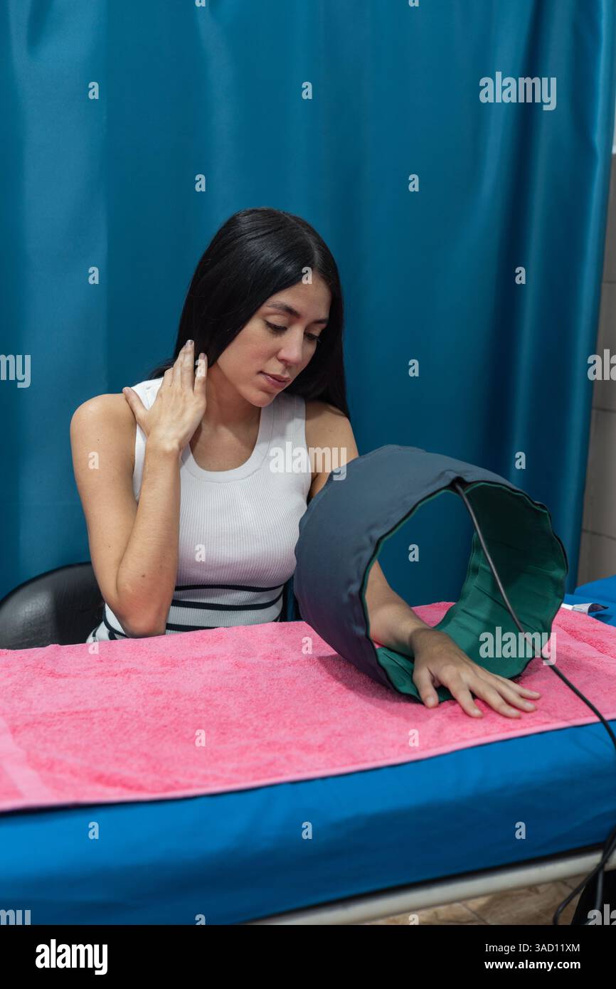 Woman undergoes wrist therapy using a magnetic field device, seated ...