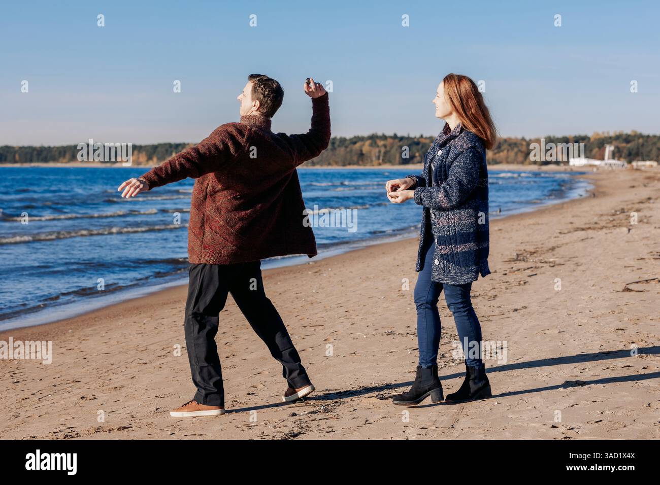 Young carefree couple in love throwing pebbles, shells, stones into sea ...
