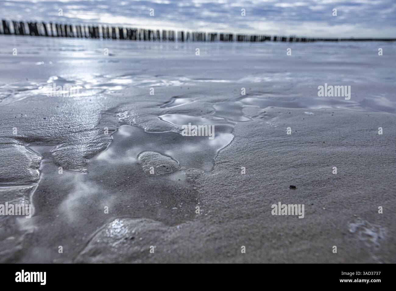 Tidal puddle on wet sandy beach at low tide and cloudy sky with a ...