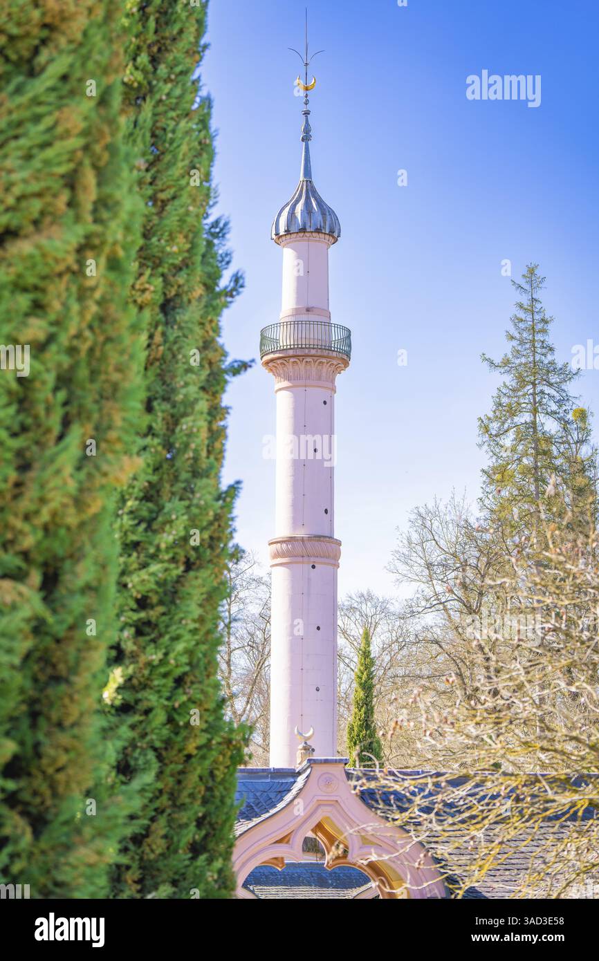 Pink minaret surrounded by green trees in front of a clear blue sky ...