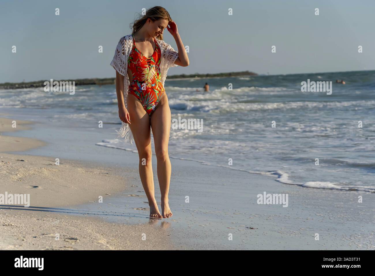 A stunning woman relaxes on the beach in a bikini that highlights her curves. She enjoys the ...