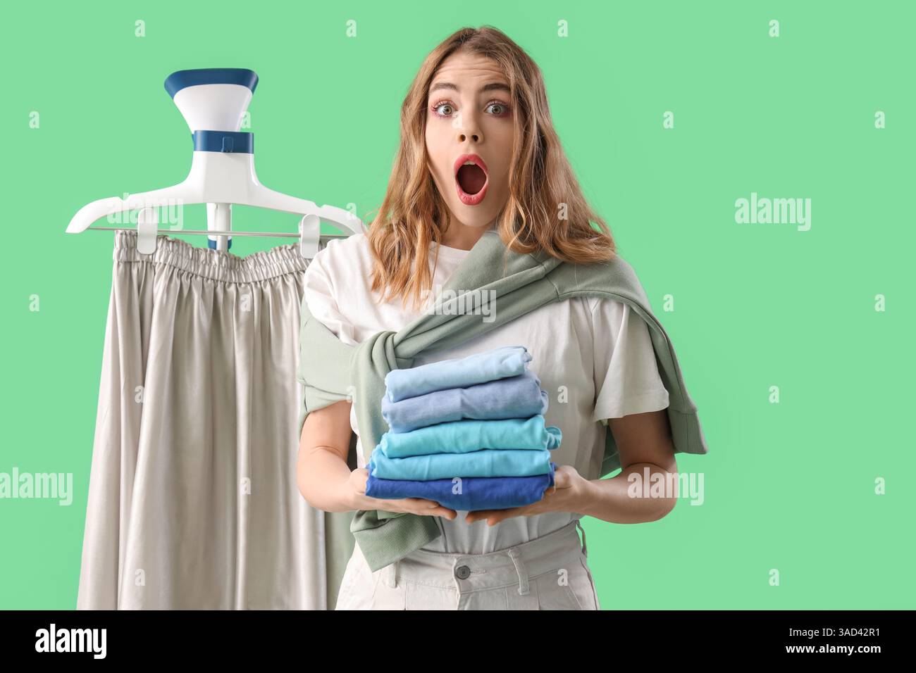 Surprised young woman with modern garment steamer and stack of clean ...