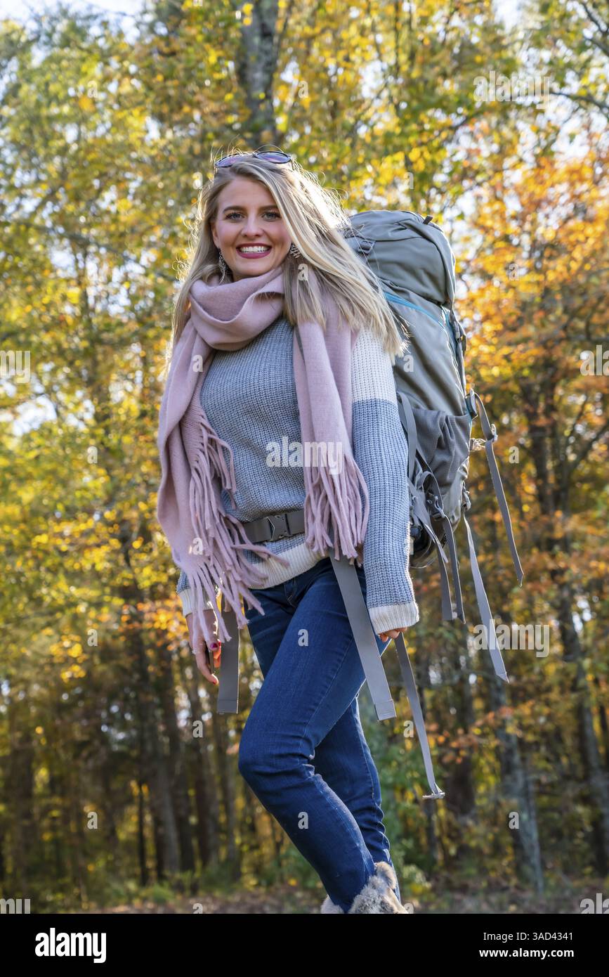 A beautiful blonde woman hikes through the autumn woods, smiling as ...