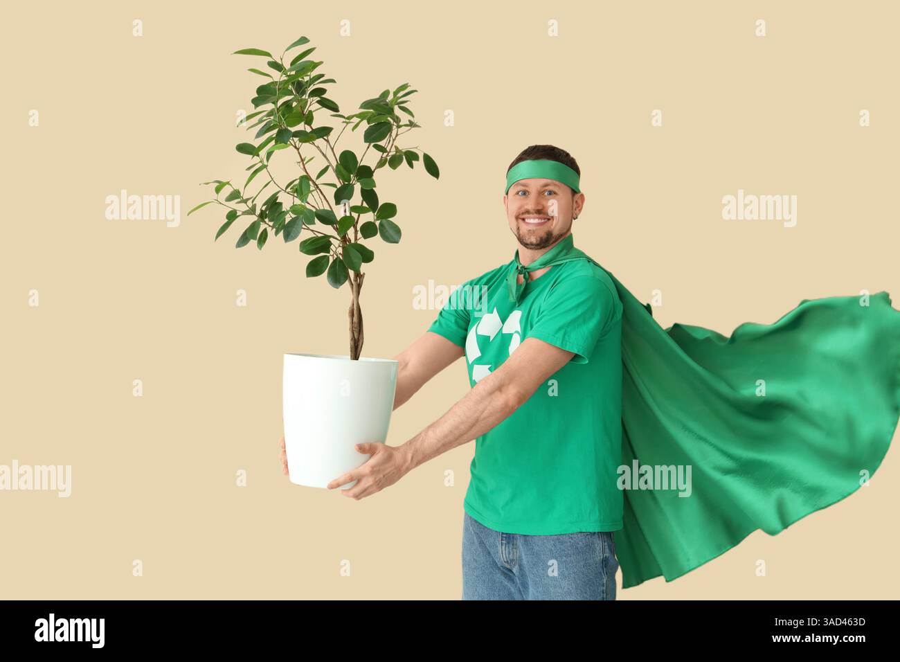 Young man dressed as eco superhero with houseplant on beige background ...