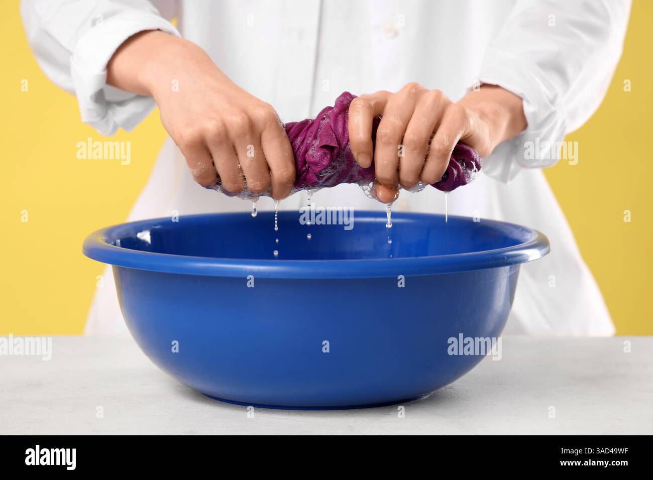 Woman wringing out wet clothes over plastic basin on white table ...