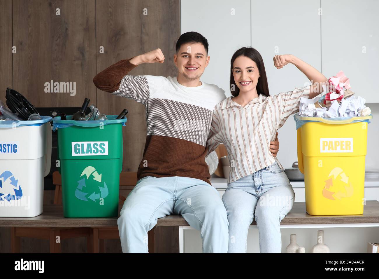 Young couple with sorted rubbish in garbage bins showing muscles at ...