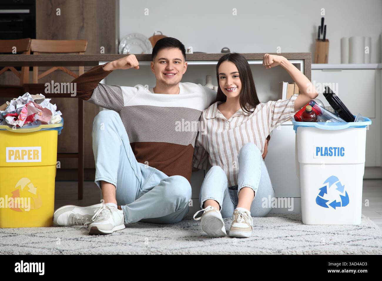 Young couple with sorted rubbish in garbage bins showing muscles at ...