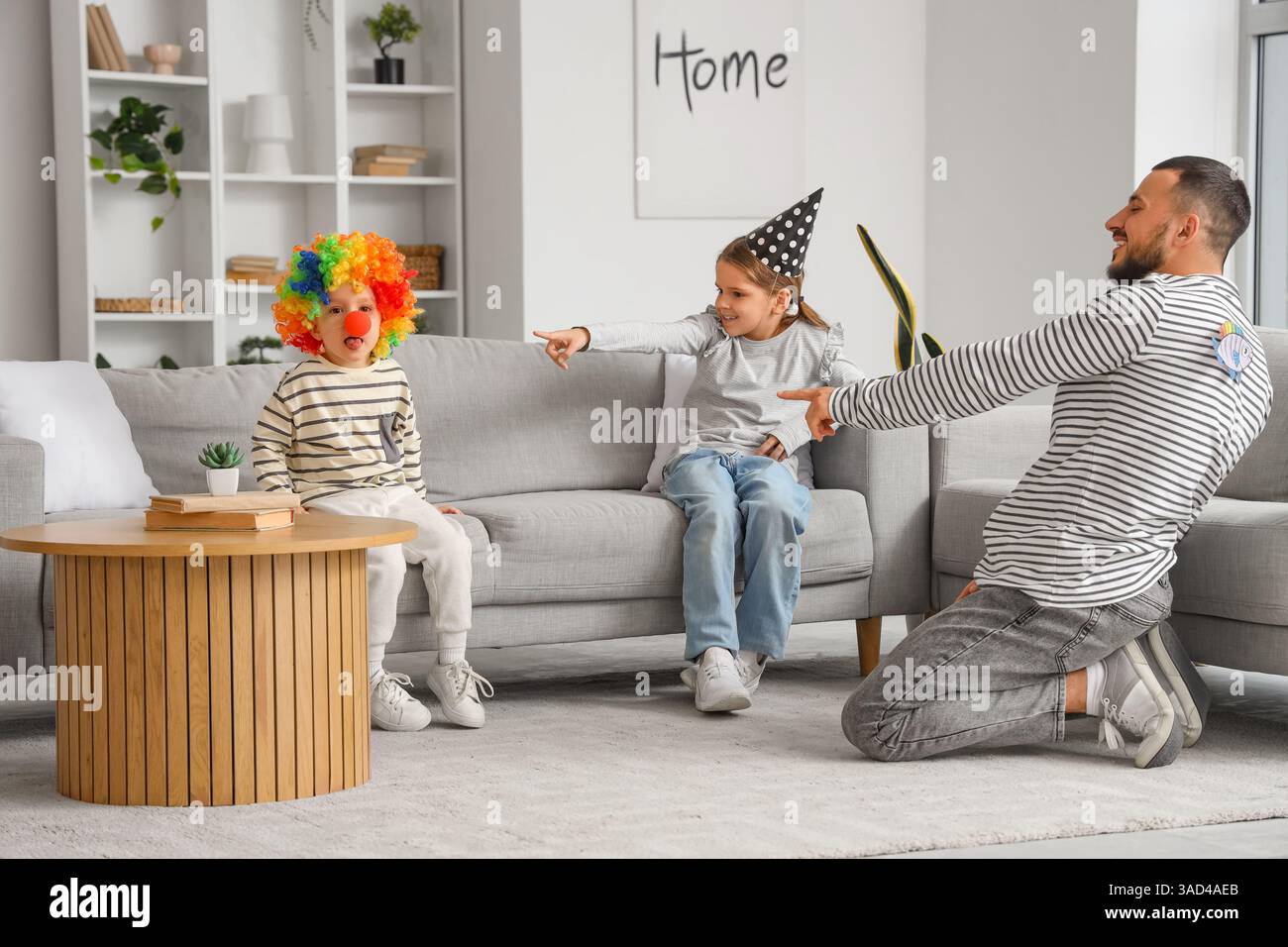 Happy father and daughter laughing at boy in clown wig at home. April ...