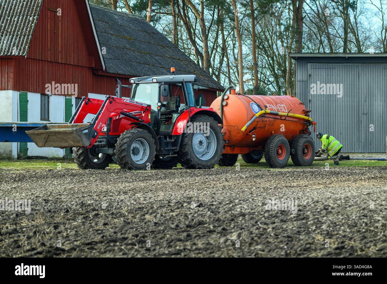 A red tractor is seen maneuvering a slurry tank across an open farm ...