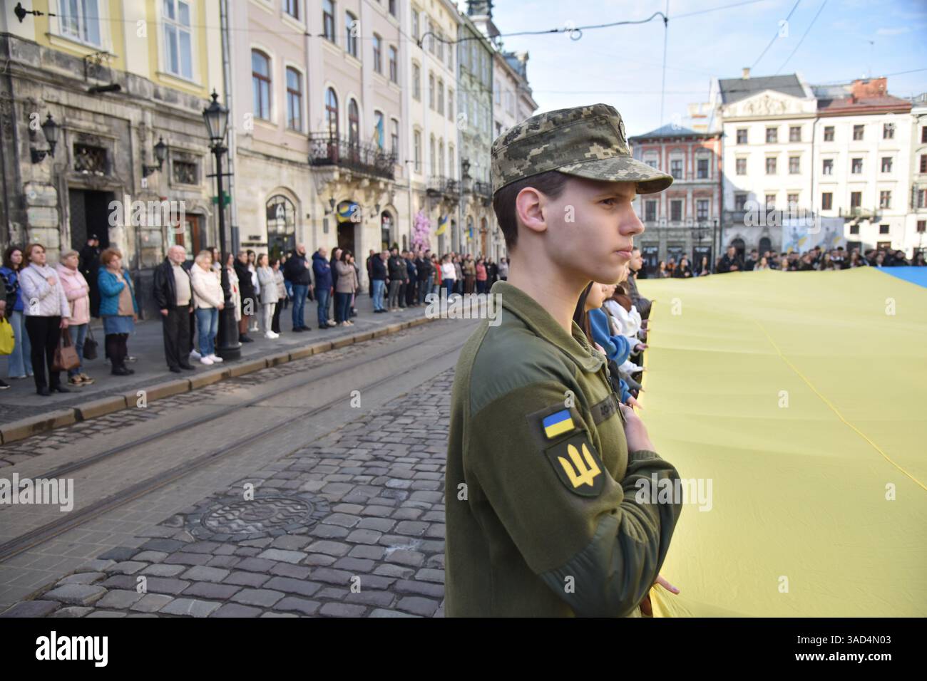 A cadet holds an unfurled large Ukrainian flag and sings the anthem during the National Anthem ...
