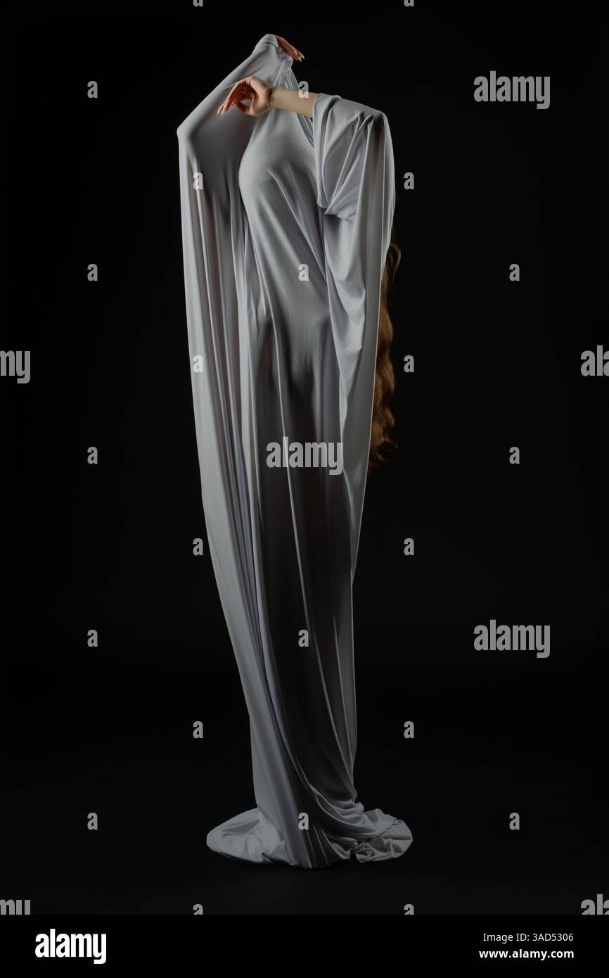 Model poses dramatically in flowing garment against black backdrop ...