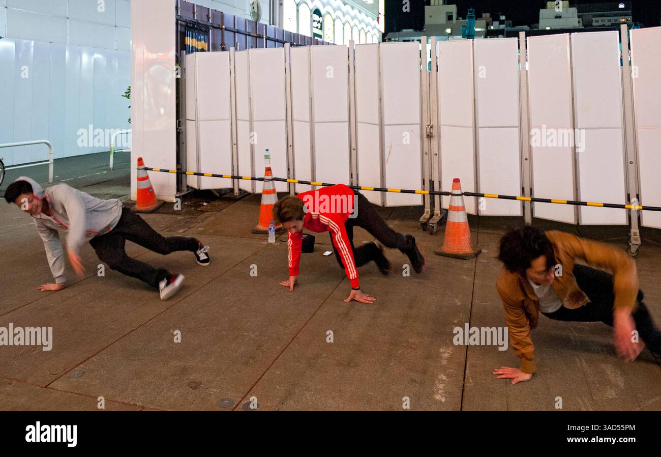 Three boys break dancing to hip-hop music at night in the street in the ...