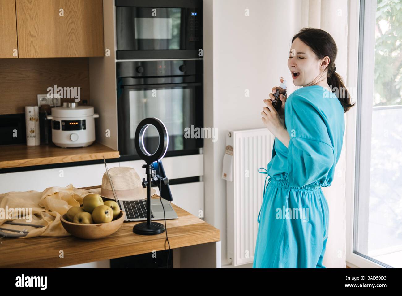Young white woman in a turquoise robe films a video in her kitchen ...