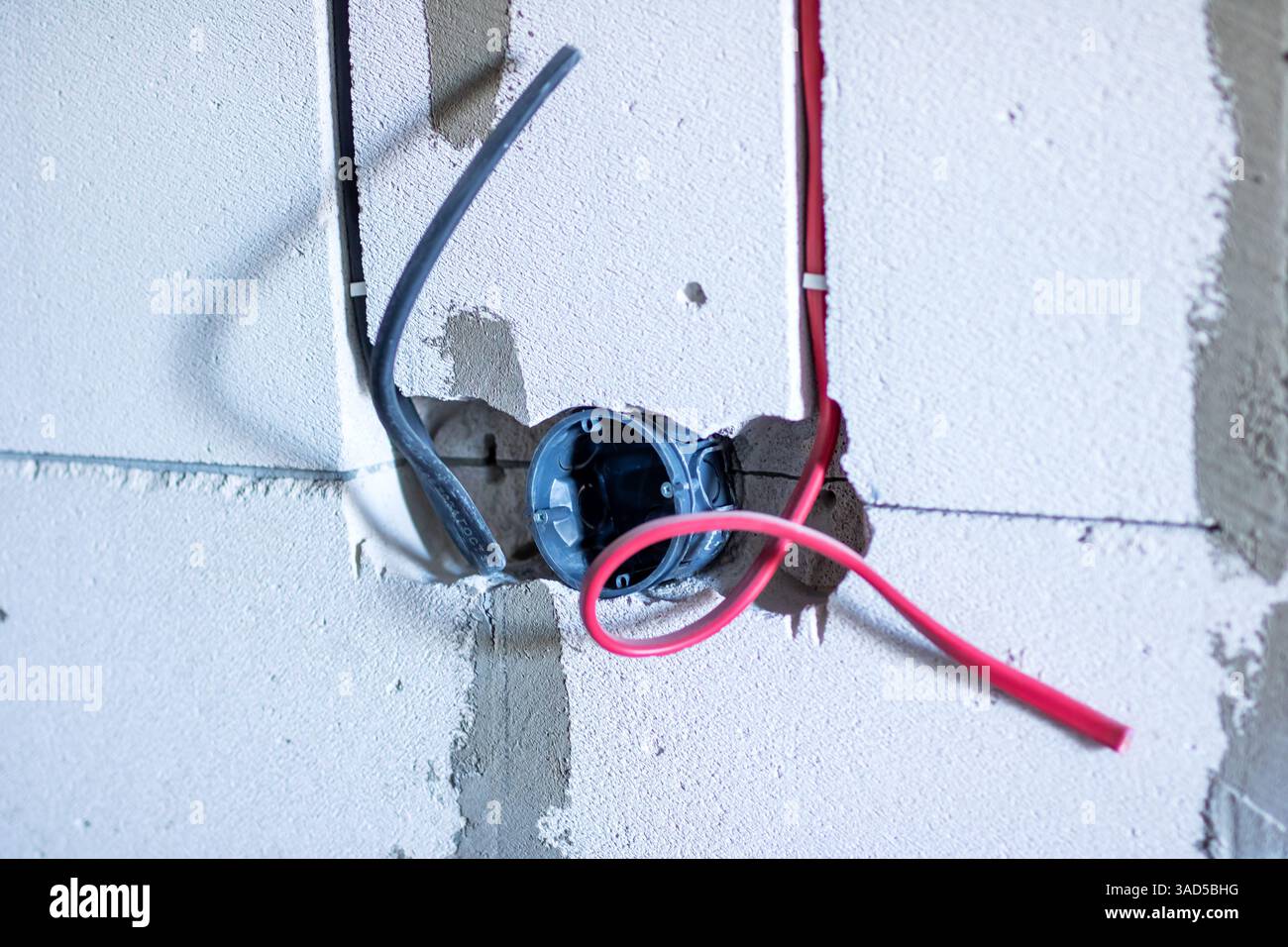A collection of various wires is protruding from an opening in the wall ...