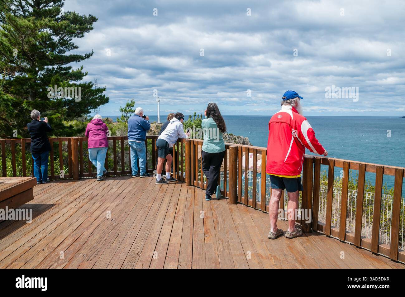 Tourists at wooden lookout deck photographing ocean view and lighthouse ...