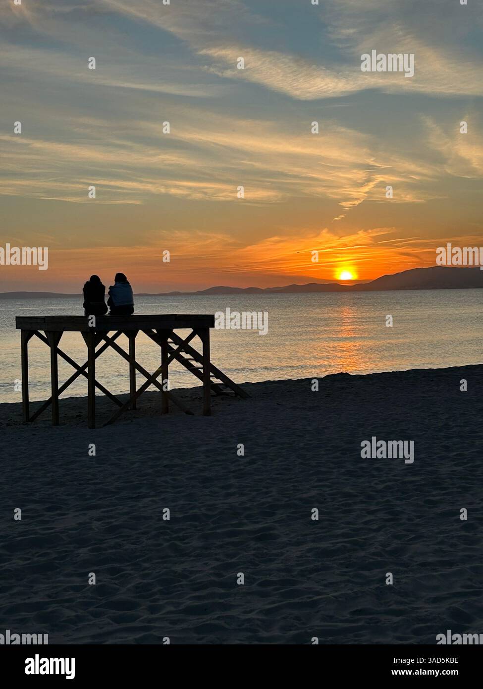 A couple sat on a lifeguard platform on the beach watching the sunset ...