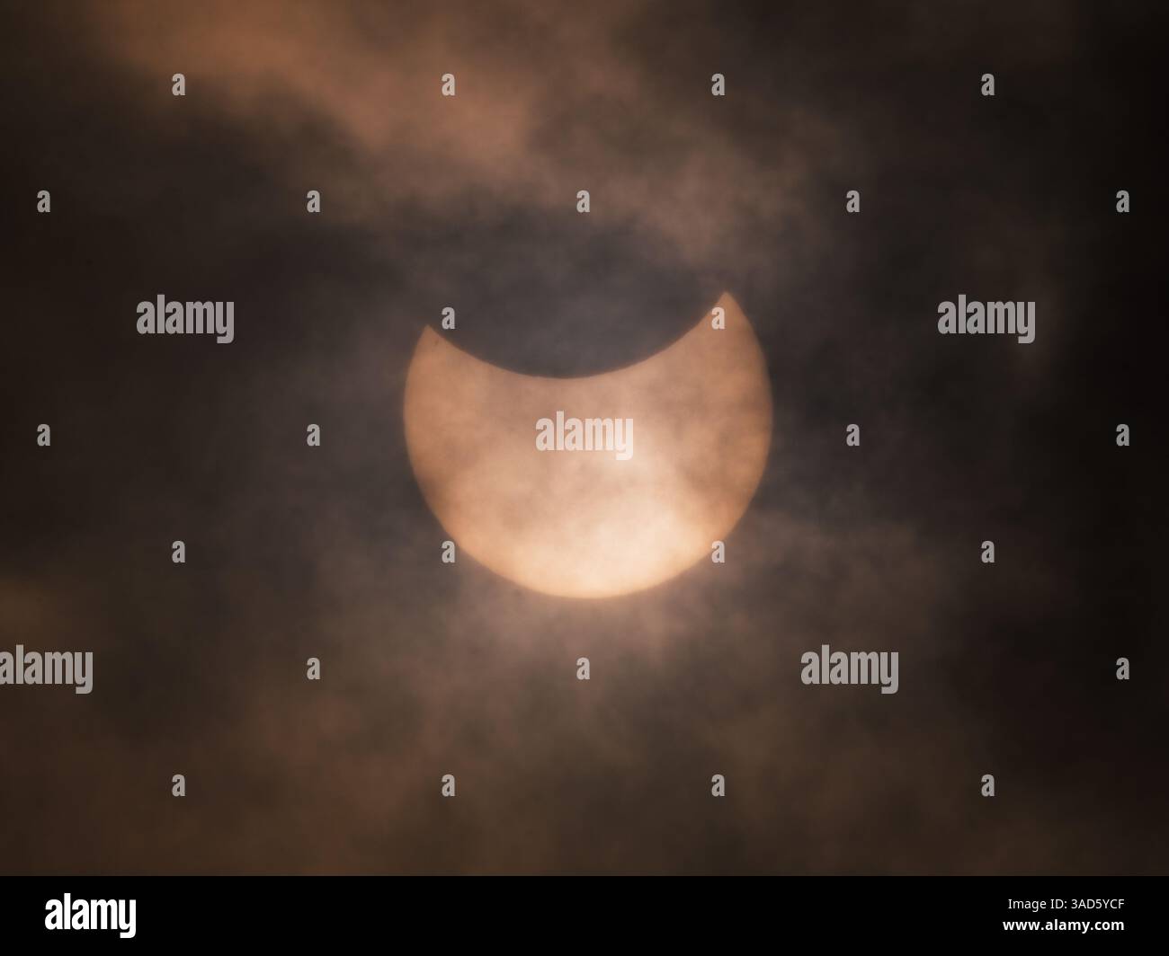 March 2025 partial solar eclipse appearing out of the clouds over ...
