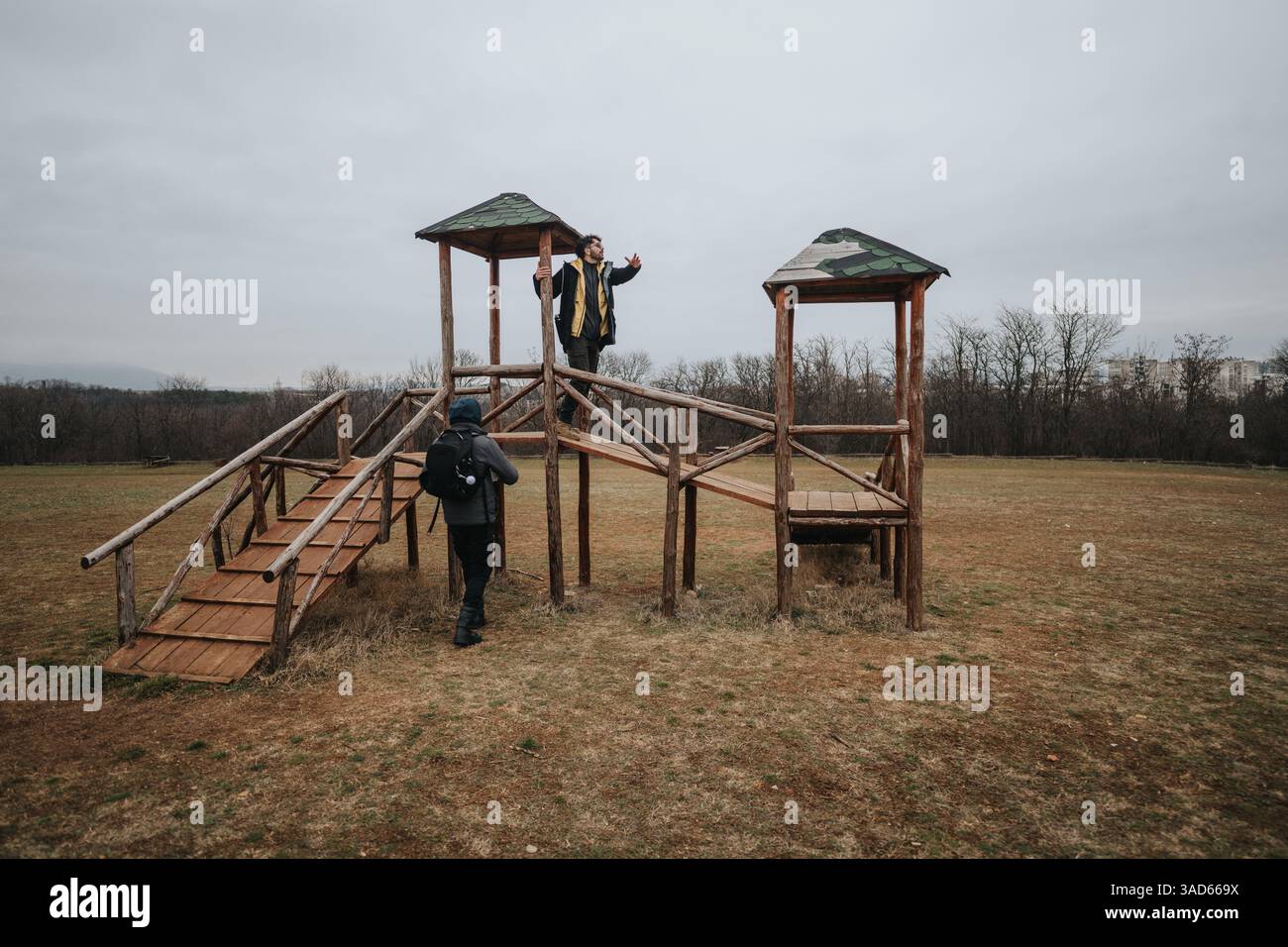 Two people exploring a wooden play structure amidst open outdoor ...