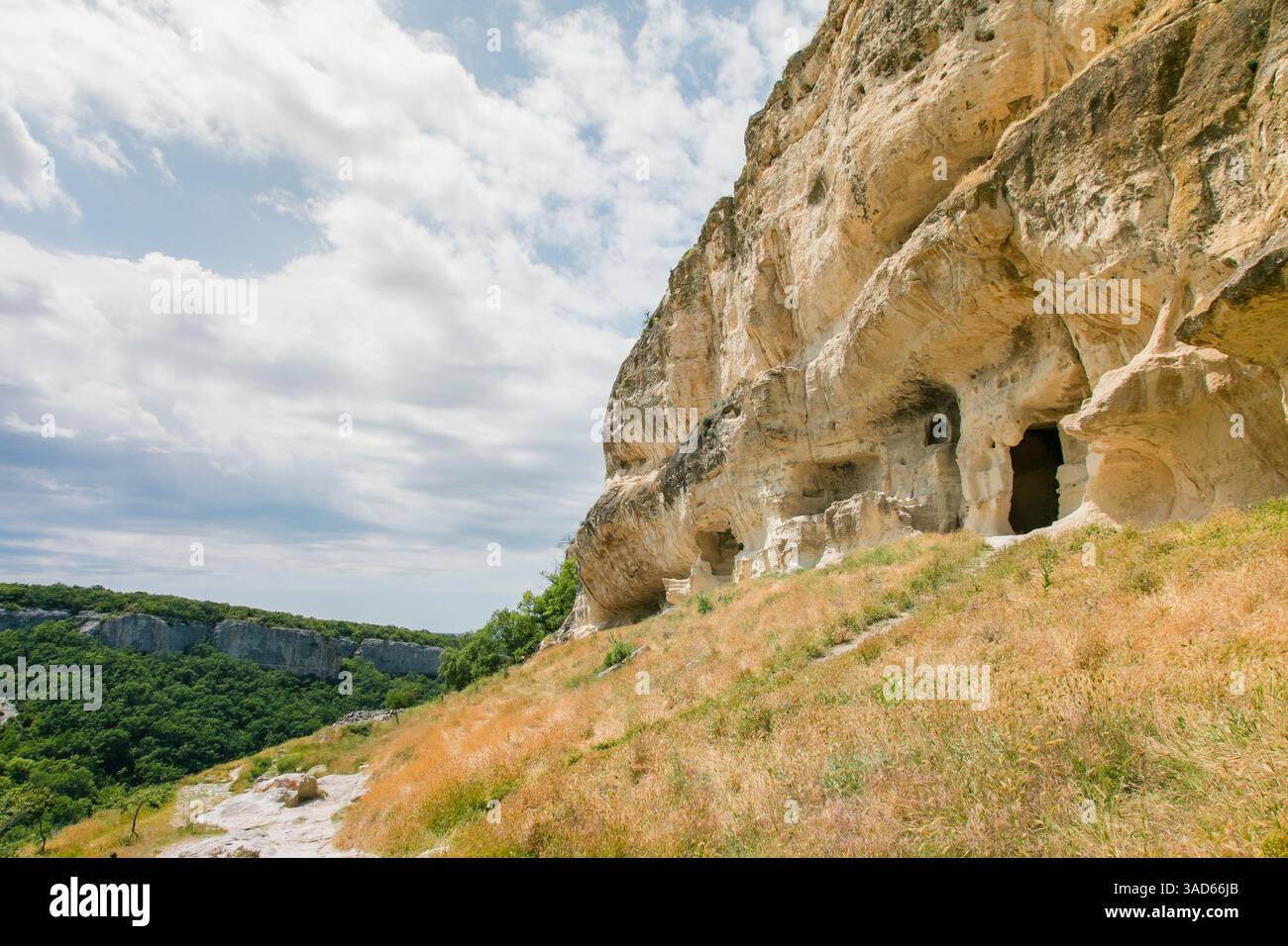 A wide-angle view of a dramatic cliffside with ancient rock caves ...