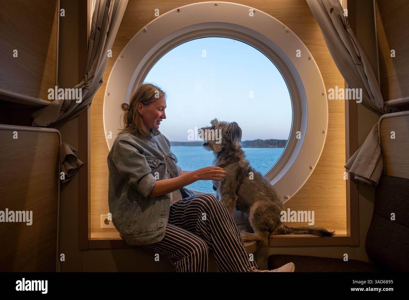 Woman sitting with dog by a round window in a cozy ship cabin Stock ...