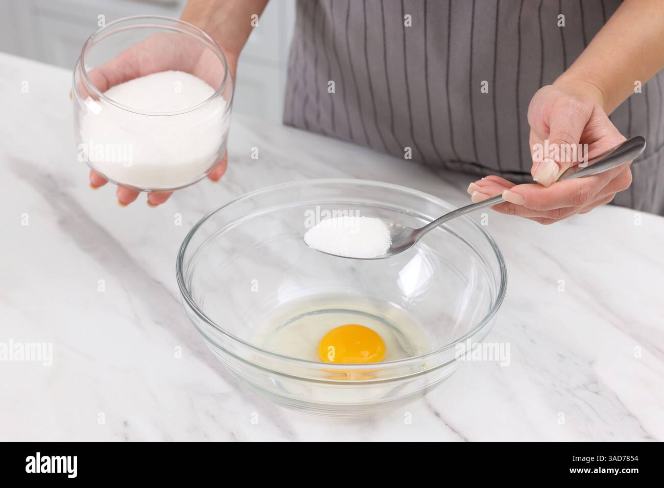 Making dough. Woman adding sugar into bowl with egg at white marble table, closeup Stock Photo ...