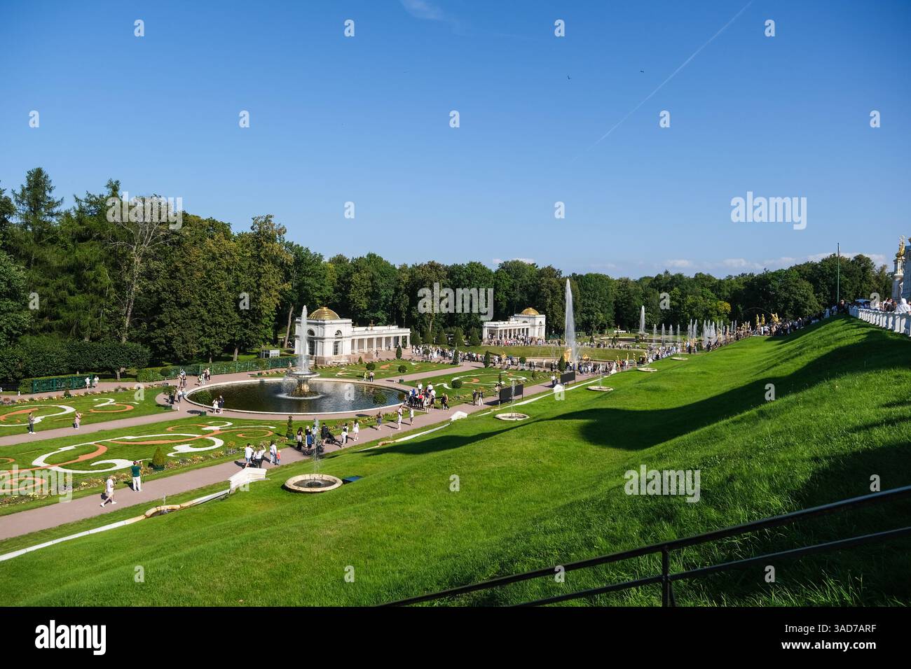 A large park with a fountain and a lot of people walking around. The ...