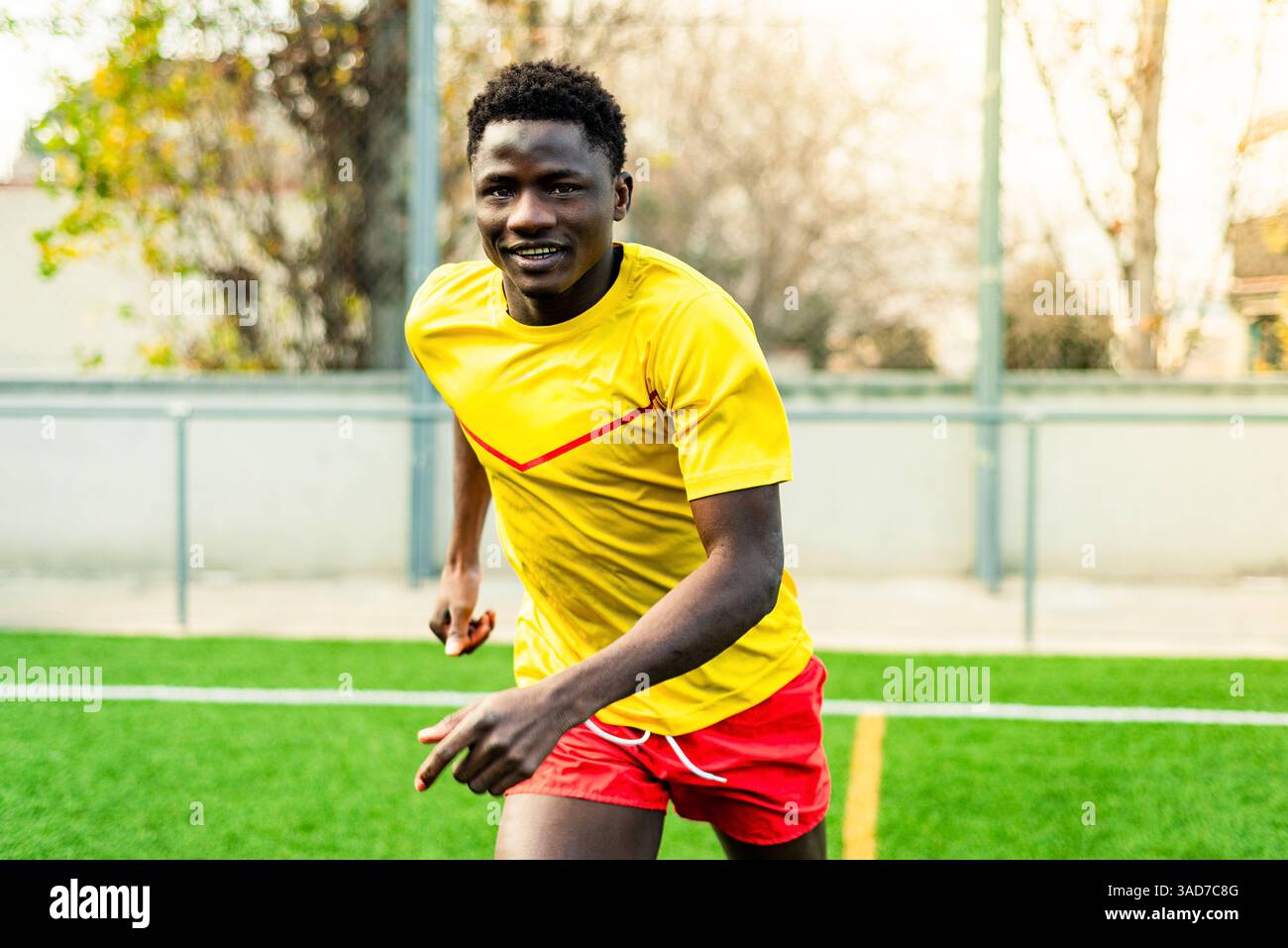 Portrait of young smiling black african man running in a football pitch ...